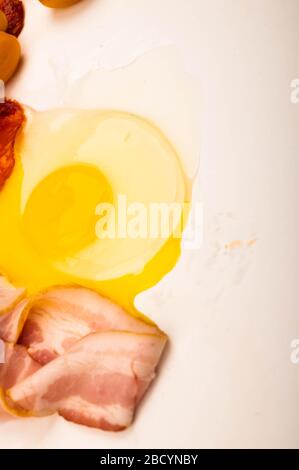A broken chicken egg without a shell, slices of sausage and bacon and ...