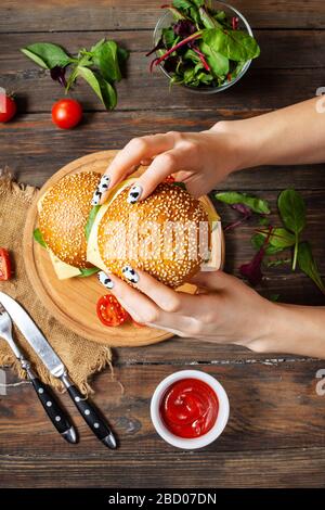 Female hands hold a delicious hamburger on a white wooden background ...