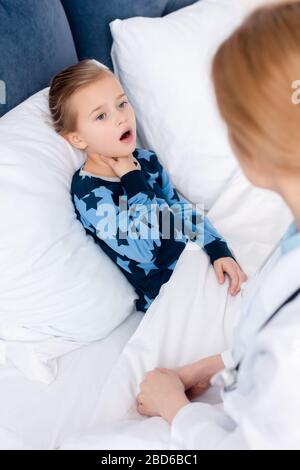 Diseased kid touching neck near mother and blurred pediatrician Stock ...