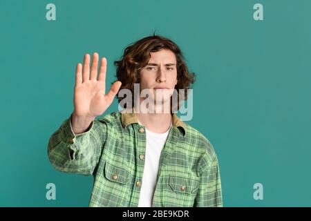 Prohibition concept. Determined young guy gesturing STOP sign on color ...