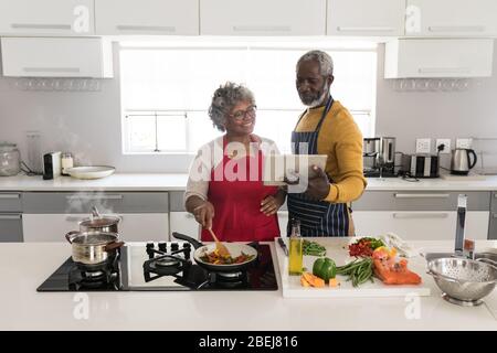 Senior african american couple cooking together in kitchen using laptop ...