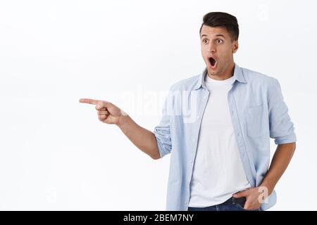 Portrait of impressed guy pointing finger left, showing smth shocking ...