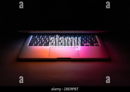 A laptop half closed in the dark with colourful glow Stock Photo - Alamy