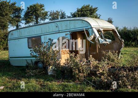 Abandoned, damaged and disused caravan in field with thistles growing ...