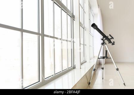 Telescope near window in modern dark room interior background, mock up ...