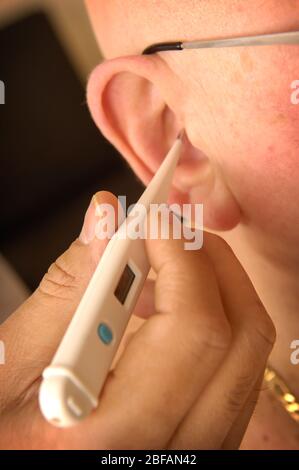 A clinician takes a patient s aural temperature with a digital thermometer Stock Photo Alamy