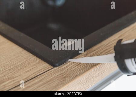 Man sealing kitchen sink joint between sink and countertop by silicone ...