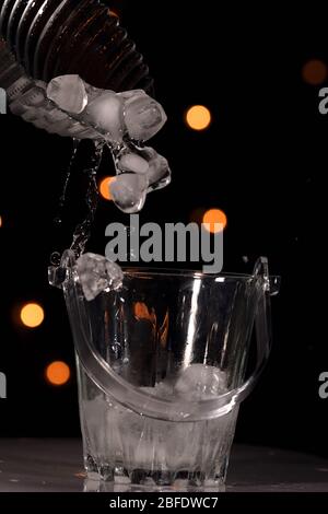 Dropping ice cubes inside ice bucket and photographed against beautiful light bokeh and isolated ...
