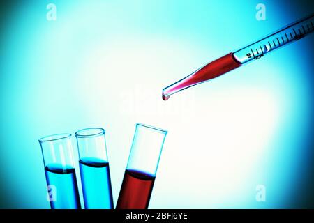 Pipette adding red fluid to the one of test-tubes on light background ...