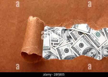 Dollars through torn craft paper Stock Photo - Alamy