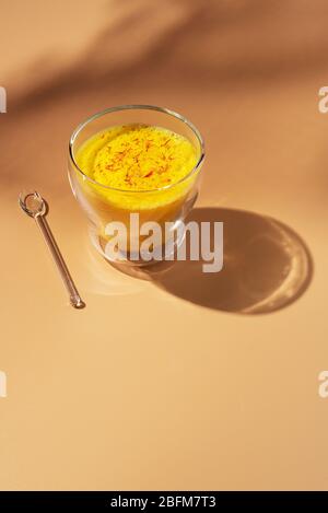 Saffron latte in a glass cup on a beige background, golden milk, hard ...