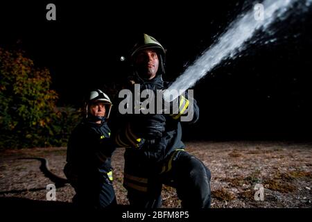 Firefighters use a water hose to eliminate a fire hazard. Team of ...