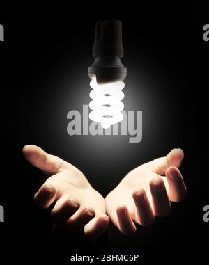 Hands with energy saving light bulb on black background Stock Photo - Alamy