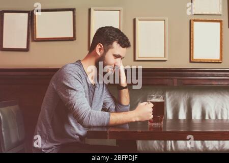 sad single man drinking beer at bar or pub, using his cellphone ...