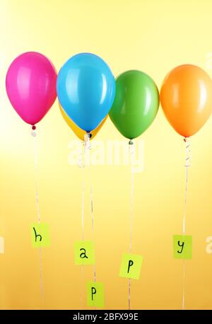 Colorful balloons keeps word happy on yellow background Stock Photo - Alamy