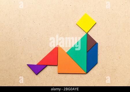 Color tangram in sitting man shape on wood background Stock Photo - Alamy