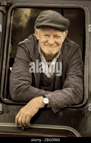 A portrait of a steam engine driver in blue overalls leaning out of the ...