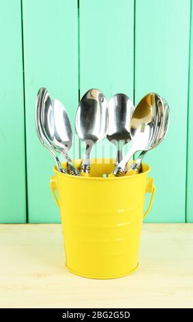 Spoons in metal bucket on color wooden background Stock Photo - Alamy