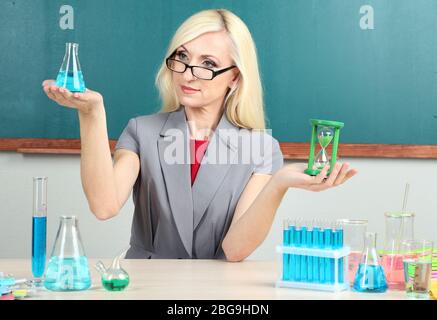 Chemistry teacher with tubes sitting at table on blackboard background ...