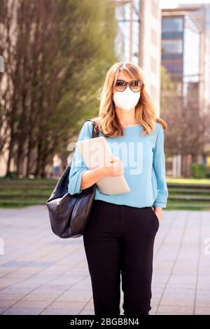 Caucasian businesswoman wearing face mask, sitting at desk, using ...