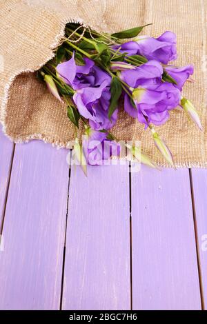 Purple artificial eustoma on sackcloth on color wooden background Stock ...