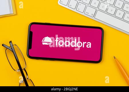 A smartphone showing the Foodora logo rests on a plain wooden table ...