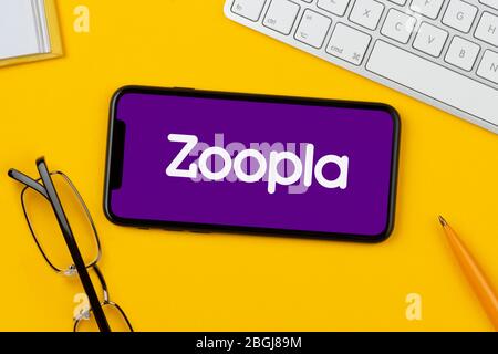 A smartphone showing the Zoopla logo rests on a plain wooden table ...