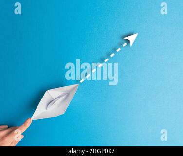 top view of hand pushing paper boat across blue background, travel and ...