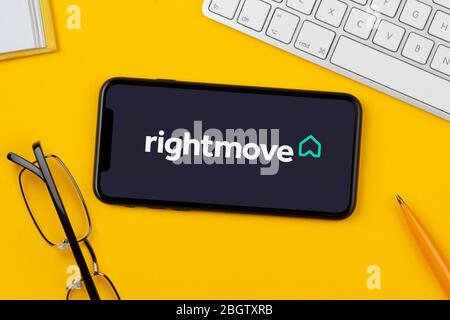 A smartphone showing the Rightmove logo rests on a plain wooden table ...