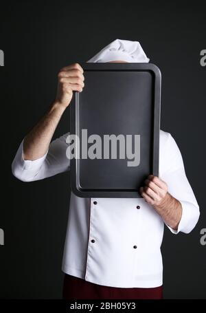 Portrait of chef with oven pan behind his face on dark background Stock ...