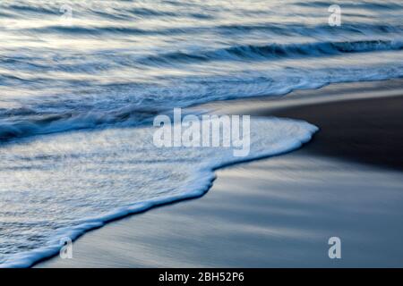 A long exposure shot of sea waves hitting the rocks located on the ...
