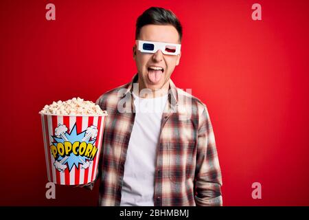 Young man eating popcorn sticking tongue out happy with funny ...