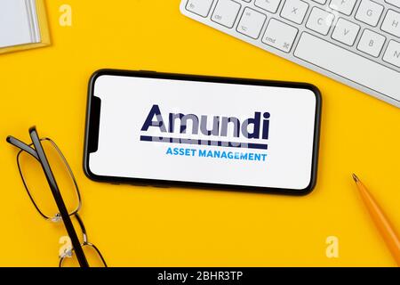 A smartphone showing the Amundi Asset Management logo rests on a plain ...