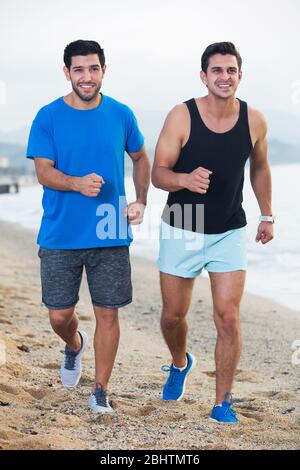Two smiling sportsmen are jogging together on the beach near sea Stock ...