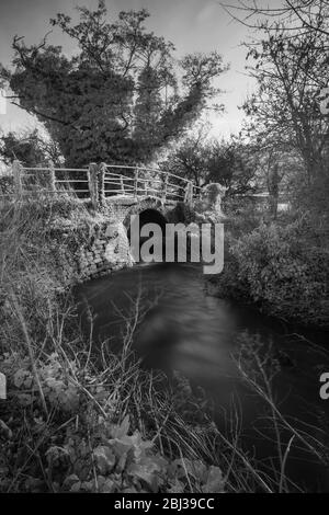 Brick footbridge over the river Stiffkey, Norfolk, England. Black and ...