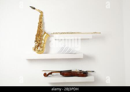 Violin, flute and saxophone on decorated shelves against white wall ...