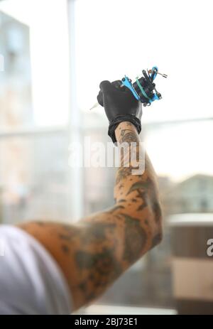 Man's hand holding tattoo machine on blurred background Stock Photo - Alamy