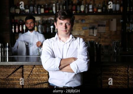 Waiter with crossed arms standing near wooden bar counter Stock Photo ...