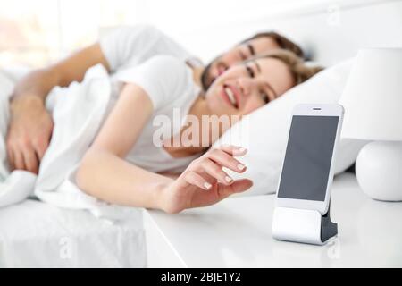Happy couple waking up with mobile alarm clock Stock Photo - Alamy
