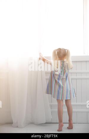 Cute little girl standing near window at home Stock Photo - Alamy