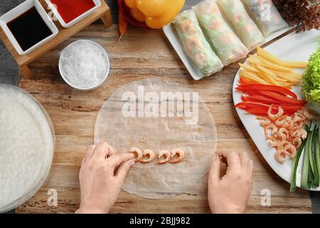 Woman preparing spring rolls in rice paper on kitchen table Stock Photo ...