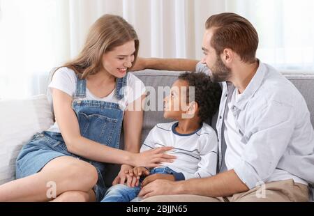 Happy couple with adopted African-American boy sitting on couch at home ...