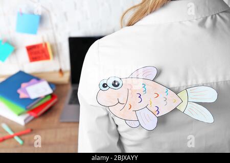 Paper fish on woman's back against yellow background, closeup. April ...