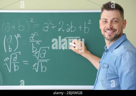 Handsome math teacher writing on blackboard in classroom Stock Photo ...
