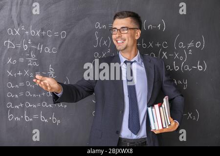 Handsome math teacher with books near blackboard in classroom Stock ...