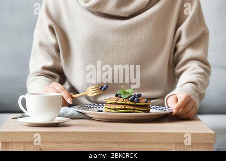 Woman eating tasty green pancakes at table Stock Photo - Alamy