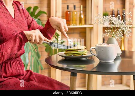 Woman eating tasty green pancakes at table Stock Photo - Alamy