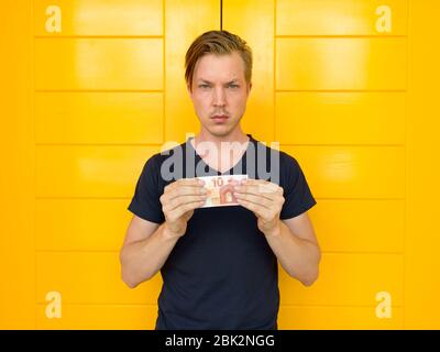 Young blond man holding euro banknotes smiling happy and positive ...