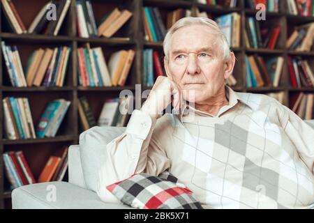 Senior man alone sitting at library in eyeglasses holding book looking ...