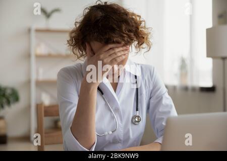 Sad and overwhelmed female doctor or nurse wearing protective face mask ...